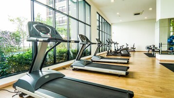 Uma academia com esteiras, bicicletas ergométricas e máquinas de remo.