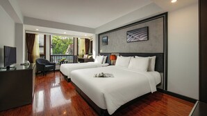 Quarto de hotel com duas camas, uma escrivaninha, televisão e varanda com cortinas.