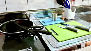 Uma bancada de cozinha com uma frigideira, tábua de corte, faca, tesoura e uma xícara de utensílios.