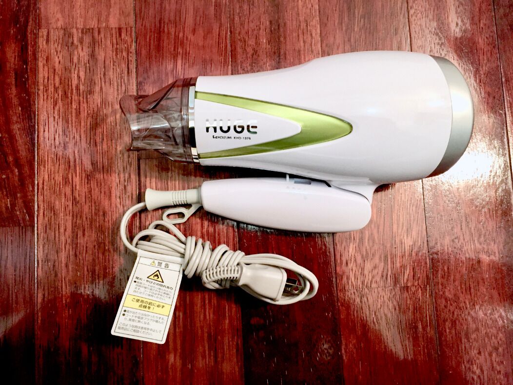 Secador de cabelo com fio elétrico e etiqueta de advertência sobre uma superfície de madeira.