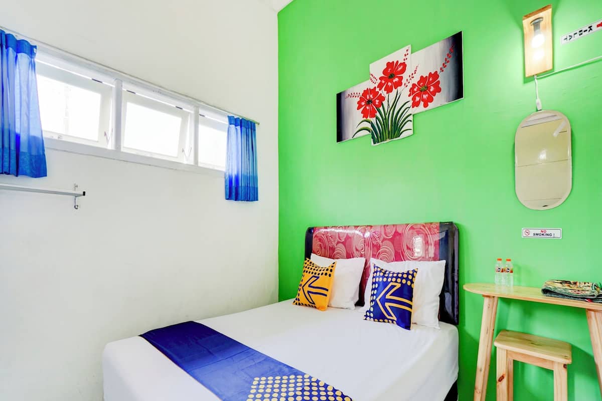 Quarto com cama, uma mesinha, um espelho e janela com cortinas azuis.