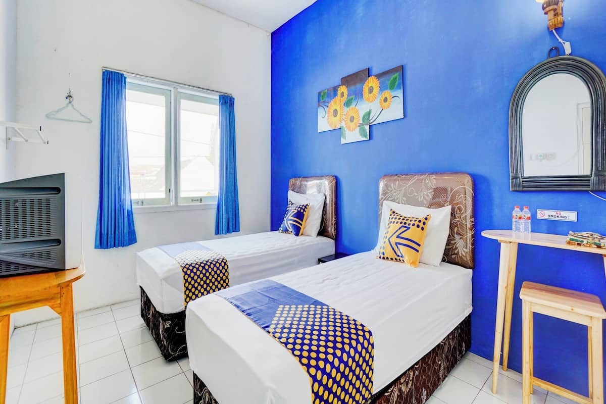 Quarto de hotel com duas camas, televisão, espelho e parede azul com ilustração de girassóis.