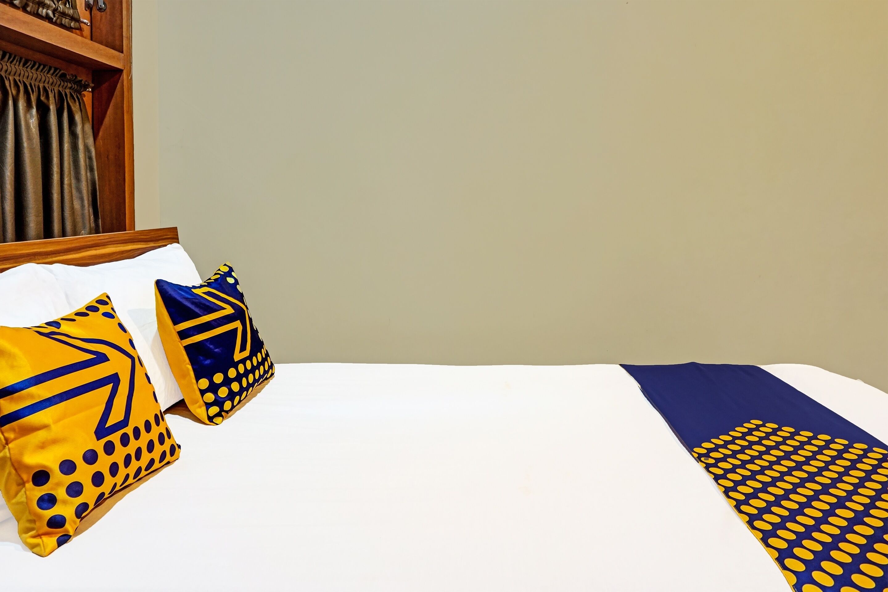 Uma cama bem arrumada com colcha branca e listras azuis, dois travesseiros com estampas em amarelo e azul, e uma cabeceira de madeira.
