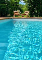 Piscina límpida com duas espreguiçadeiras de madeira e vegetação exuberante ao fundo.