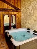 Um salão de spa de madeira com hidromassagem, vigas de madeira e parede de pedra.