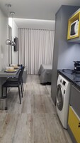 Quarto de hotel compacto com área de refeições, máquina de lavar e cama com colcha cinza.