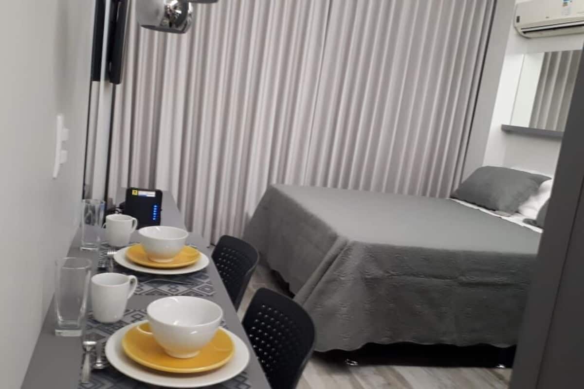 Quarto de hotel com uma cama, uma mesa de jantar com cadeiras e uma pequena área de cozinha.