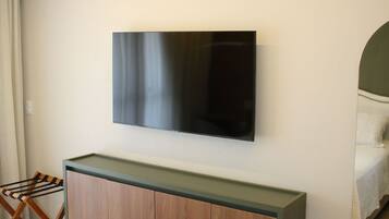 Quarto de hotel moderno com televisão de tela plana presa a um console de madeira, cama com edredom branco e um espelho grande refletindo a cama.