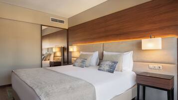 Quarto de hotel moderno com uma cama grande, mesas de cabeceira, um espelho e um painel de cabeceira de madeira.