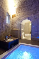 Quarto com paredes de pedra, uma banheira de hidromassagem, porta de madeira e uma pequena janela.