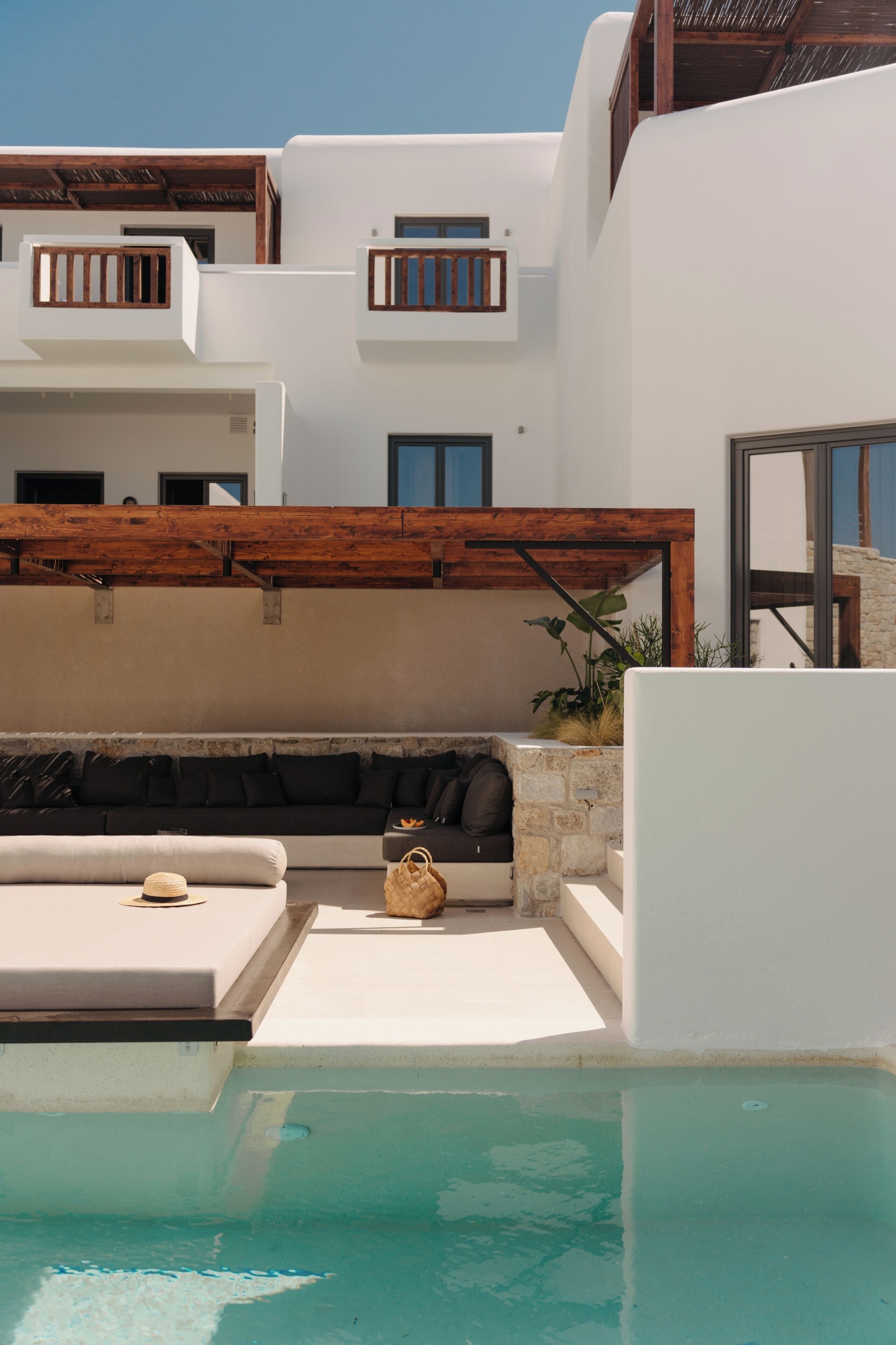 Uma área moderna com piscina ao ar livre, um banco de pedra e um pérgula de madeira.