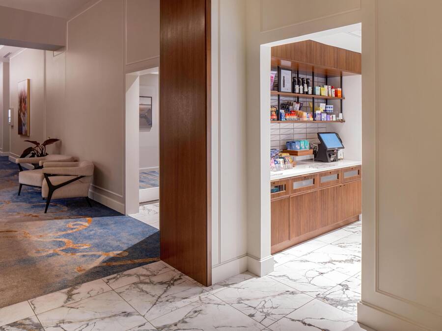 Um hall de hotel com piso de mármore, balcão de recepção, área de estar com sofá e uma grande janela.