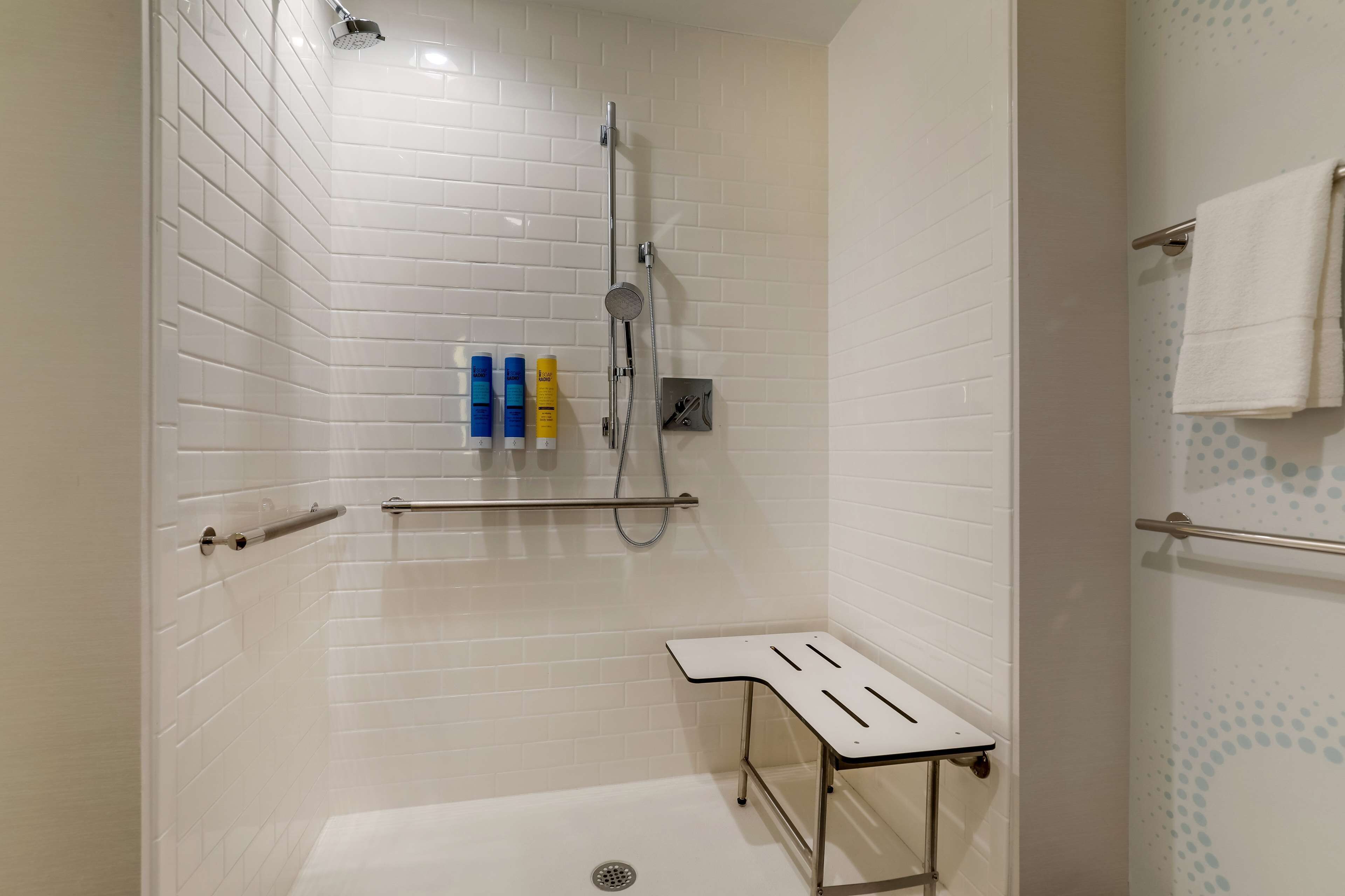 Um chuveiro moderno com paredes revestidas de azulejos brancos, um chuveiro manual e um acessório de chuveiro manual. Há dois frascos de shampoo e condicionador na parede.