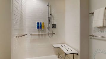 Um chuveiro moderno com paredes revestidas de azulejos brancos, um chuveiro manual e um acessório de chuveiro manual. Há dois frascos de shampoo e condicionador na parede.