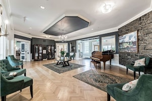 Uma sala de estar espaçosa com piso de madeira em padrão herringbone, um piano de cauda e uma parede de destaque em pedra.