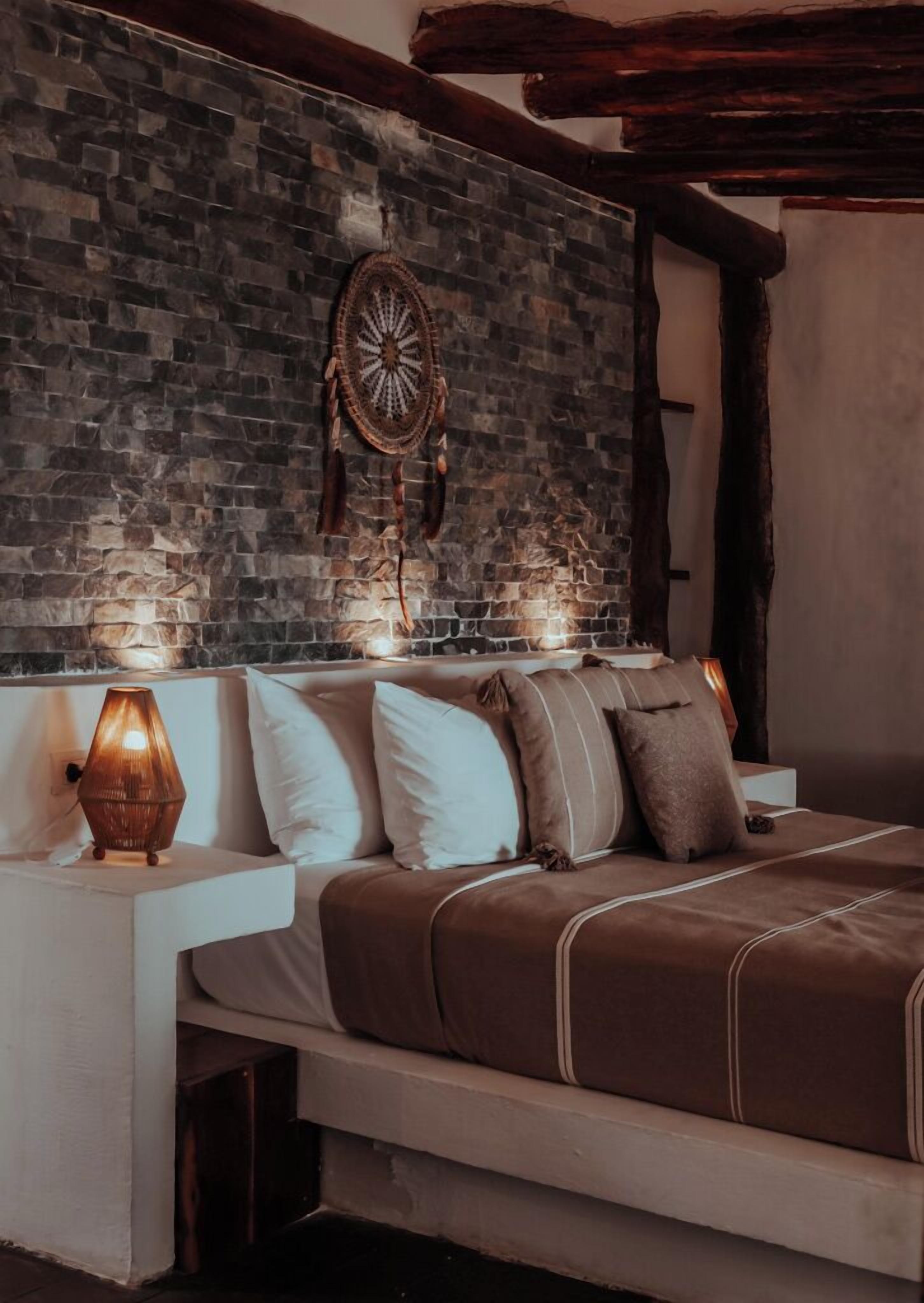 Quarto com parede de pedra, um sonho apanhador e uma cama com almofadas e manta.
