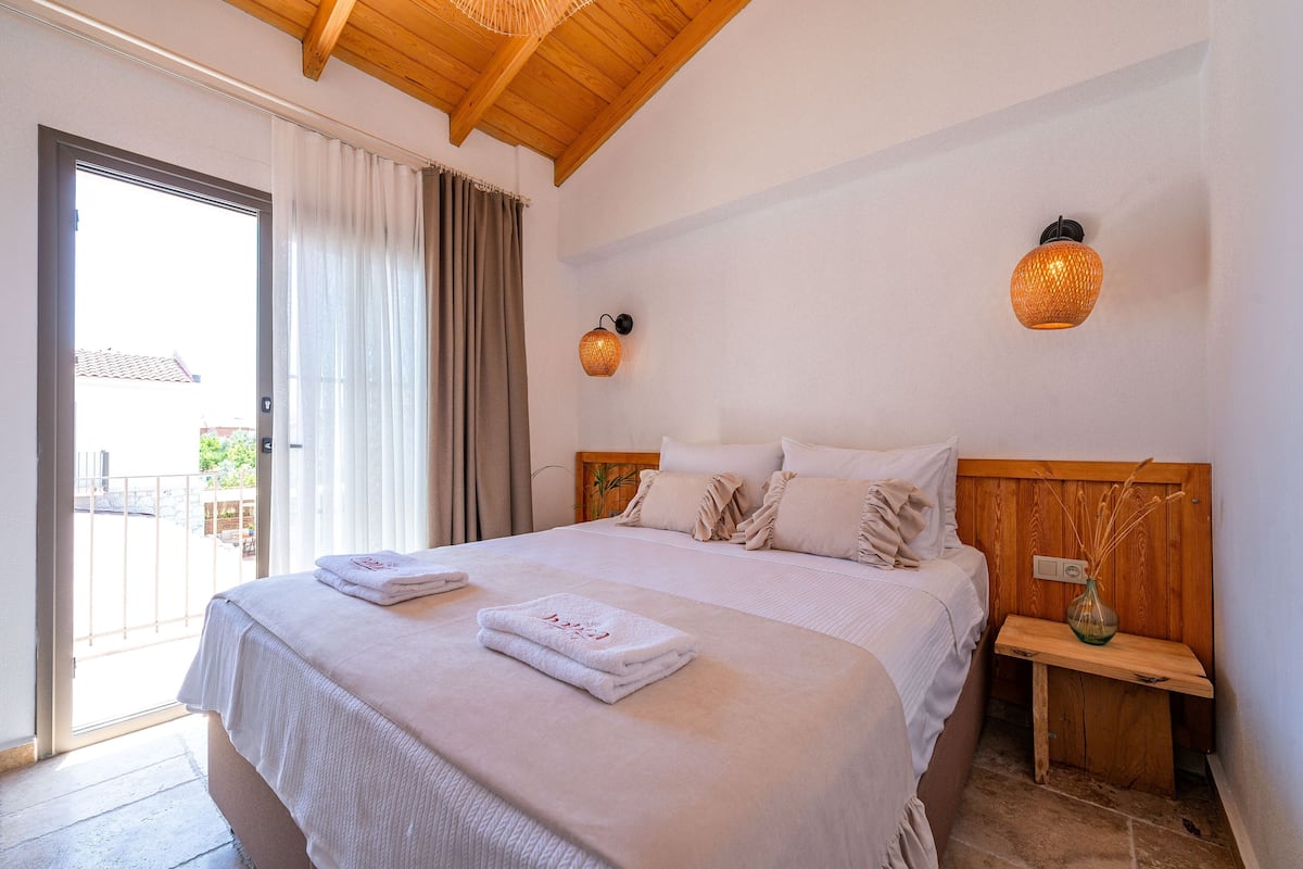 Quarto com cama, mesa de cabeceira, abajur e vista para o exterior.
