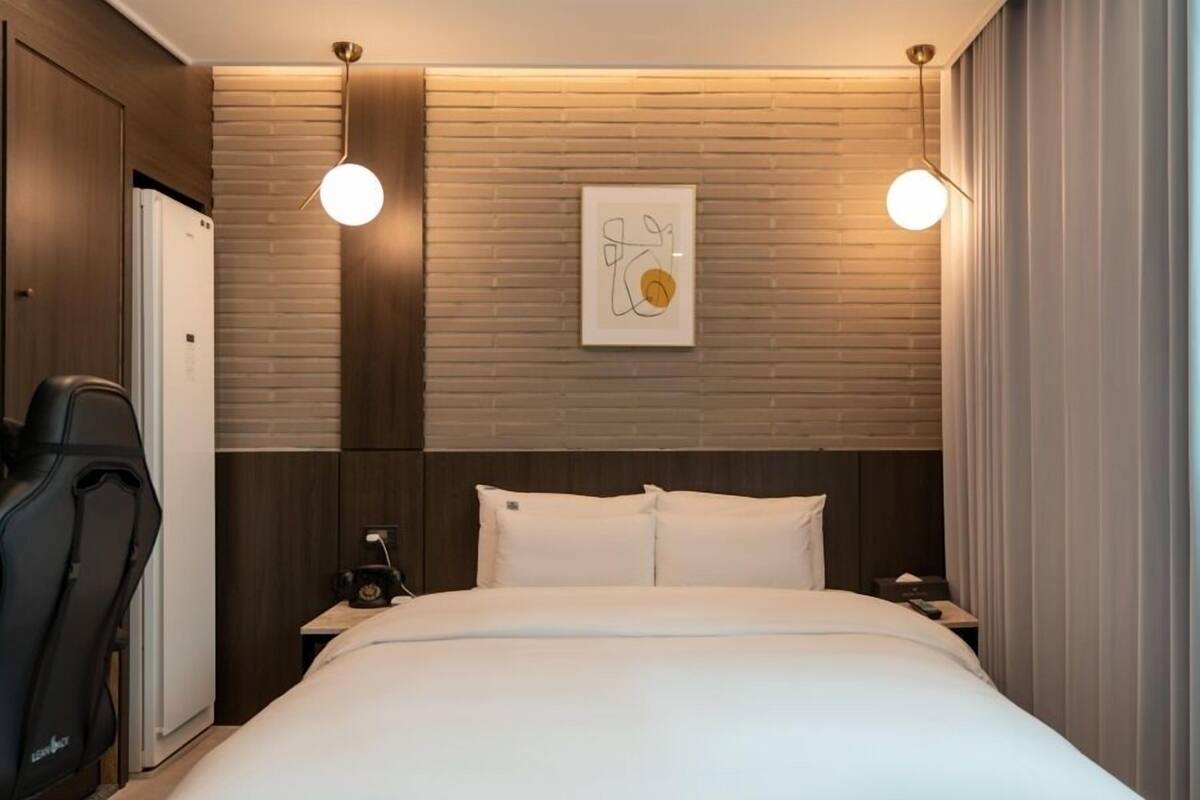 Quarto de hotel moderno com cama, mesas de cabeceira, telefone e uma obra de arte pendurada na parede.