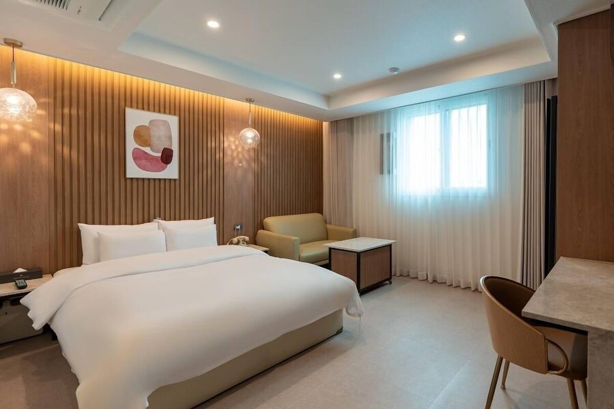 Quarto de hotel moderno com uma cama grande, uma escrivaninha, uma cadeira e um sofá.