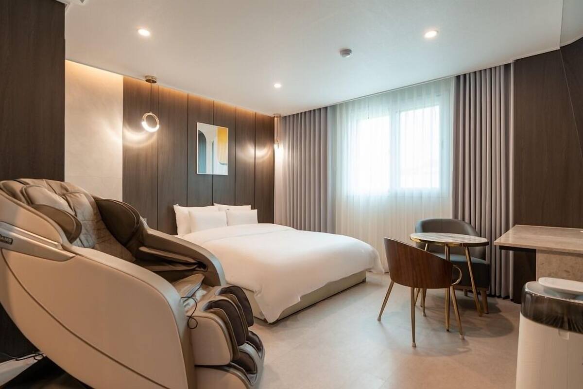 Quarto de hotel com cama, poltrona de massagem, escrivaninha e televisão.