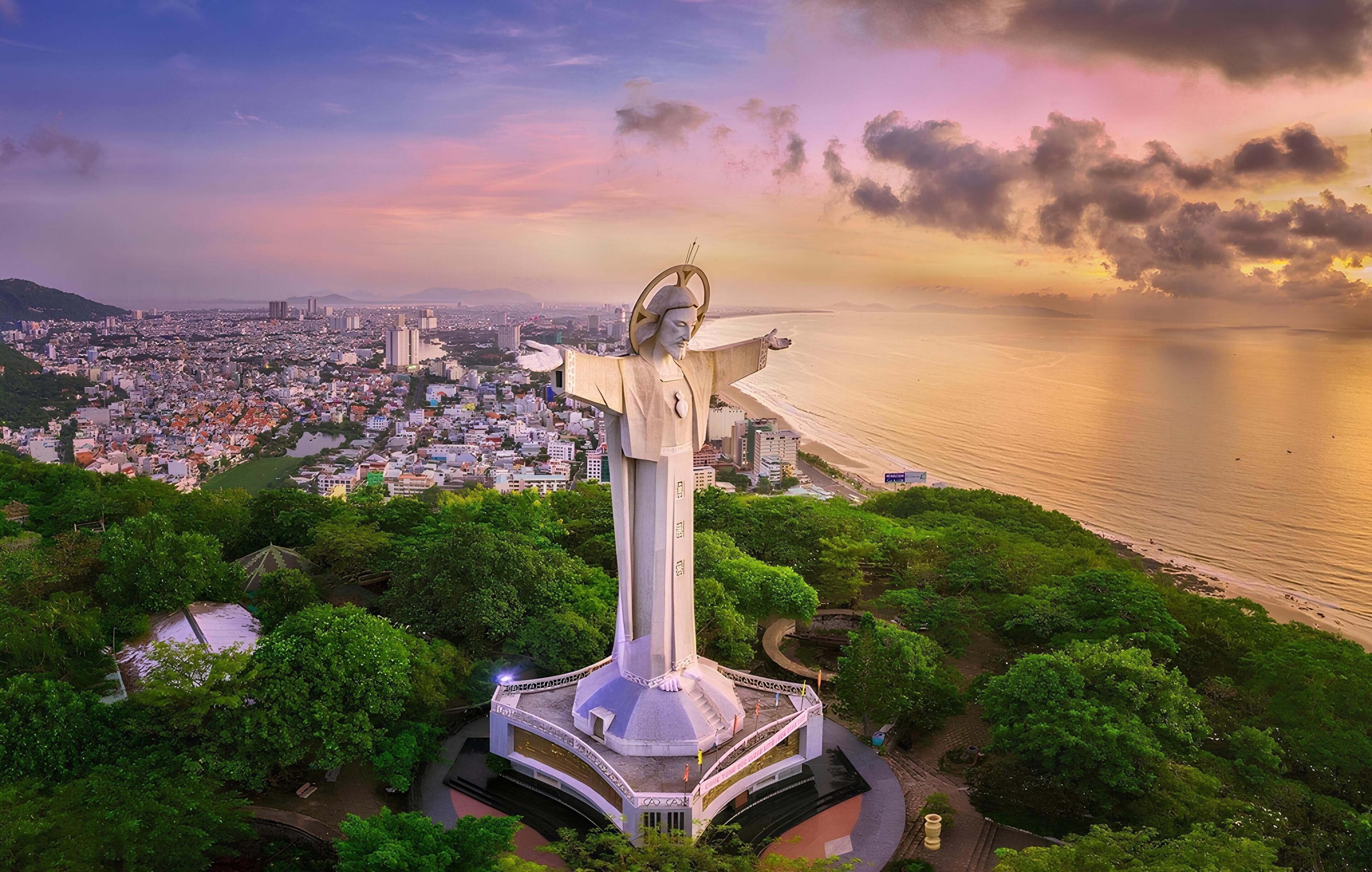 Uma estátua imponente com braços estendidos, com vista para a paisagem urbana costeira.
