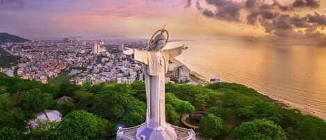 Uma estátua imponente com braços estendidos, com vista para a paisagem urbana costeira.