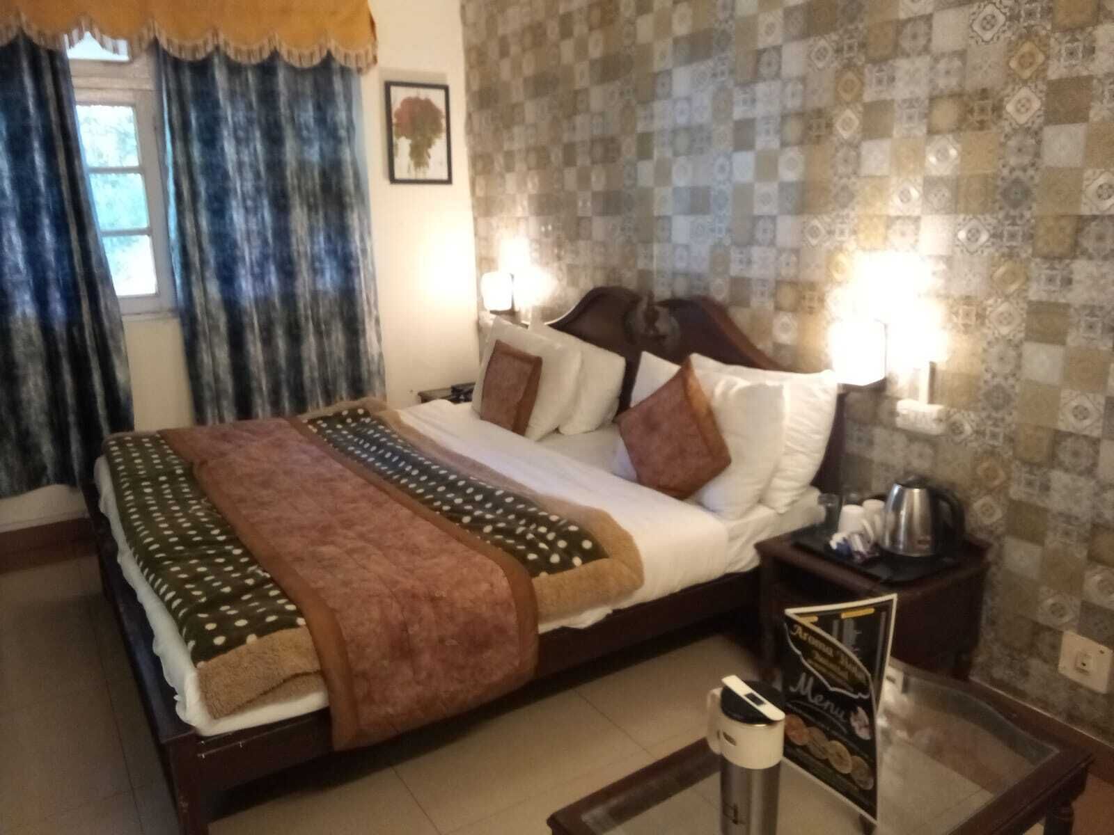 Quarto de hotel com uma cama, mesa de cabeceira, cafeteira e um quadro na parede.