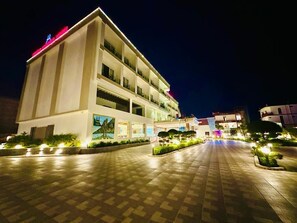 Hotel com vários andares e pátio central, iluminado por luzes no chão.