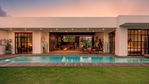 Uma casa moderna com piscina, deck de madeira e área de refeições com mobiliário para área externa.