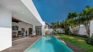 Uma área moderna com piscina ao ar livre, deck de madeira, espreguiçadeiras e água azul cristalina.