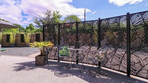 Uma área de pátio com cerca de metal decorativa, móveis de exterior e plantas em vasos.
