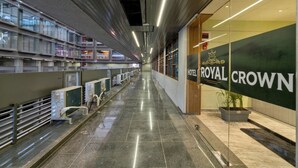 Um corredor com parede de vidro de um lado e um letreiro do hotel 'ROYAL CROWN' do outro.