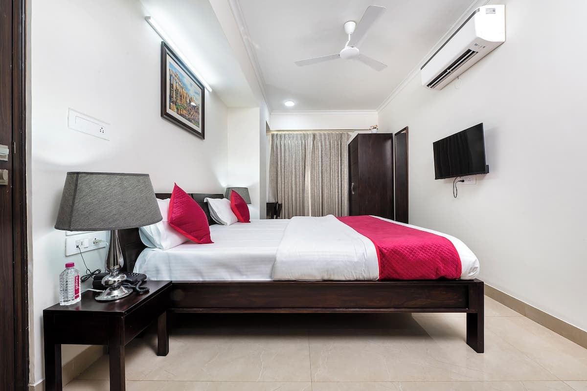 Quarto de hotel com cama, mesa de cabeceira com abajur, TV fixada na parede e aparelho de ar condicionado.