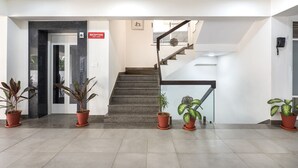 Uma área de recepção com escada, plantas em vasos e uma placa indicando que a recepção fica no primeiro andar.