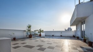 Um terraço no telhado com piso xadrez, plantas em vasos e vista clara do horizonte da cidade.