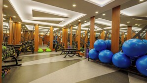 Uma academia com equipamentos de exercícios, pilares de madeira e bolas de ginástica azuis.