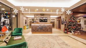 Um hall de hotel com balcão de recepção, assentos verdes, um pinheiro de Natal e uma tela grande.