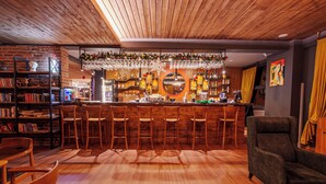 Uma área de bar com banquetas de madeira, uma estante de livros e um candelabro.