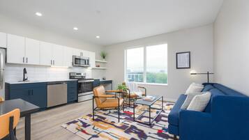 Um apartamento moderno com cozinha, sala de jantar e sala de estar. Apresenta armários brancos, um sofá azul e um tapete colorido.