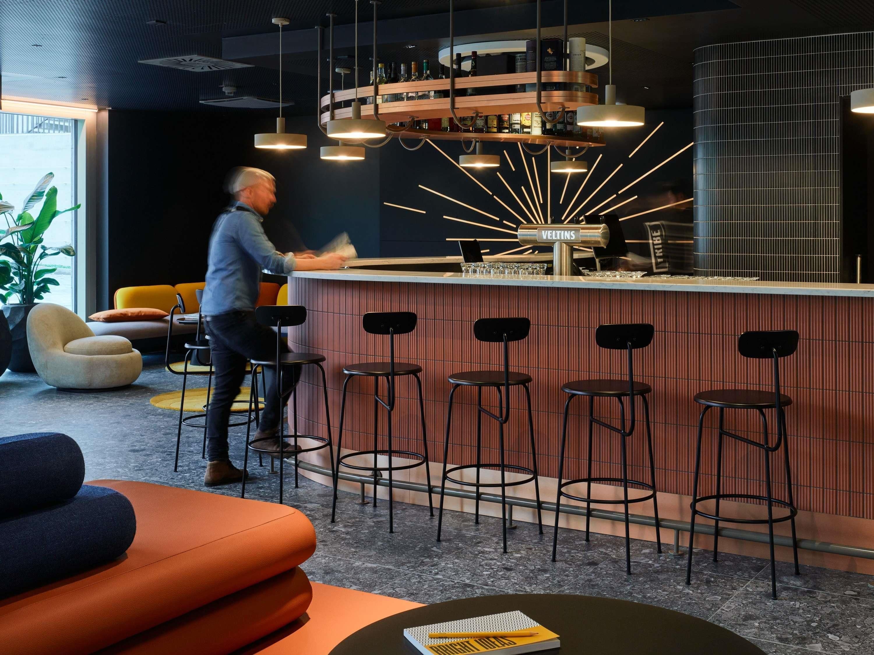 Uma área de bar moderna com balcão, banquetas e luminárias pendentes.