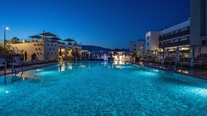Piscina com revestimento em azulejos, rodeada por espreguiçadeiras e guarda-sóis, com edifícios ao fundo.