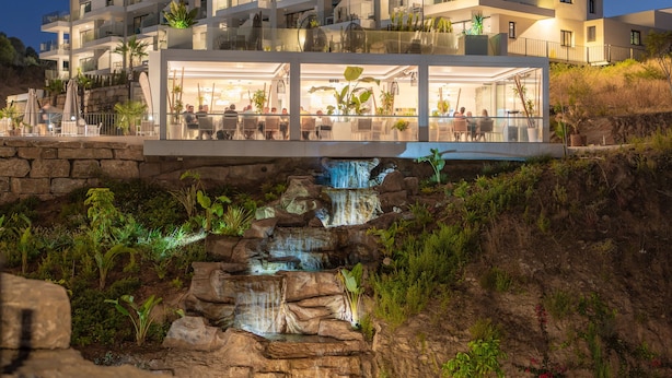 Um hotel com vários andares, varandas, área de refeições e uma cascata.