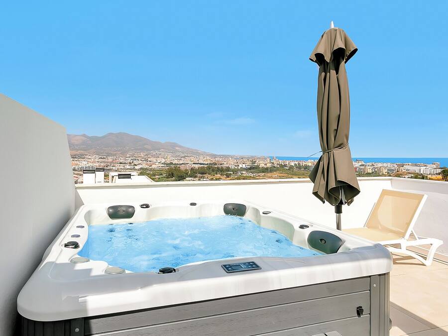 Uma banheira de hidromassagem com vista para a cidade, um guarda-sol e uma espreguiçadeira em um terraço.