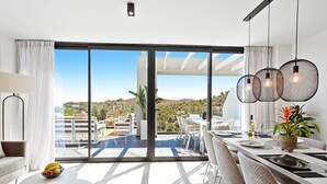 Uma área de jantar moderna com uma grande porta de vidro que dá para um terraço, mobiliário branco e um vaso com planta.