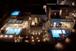 Um imóvel residencial moderno, com vários níveis, duas piscinas, áreas de estar ao ar livre e uma parede de pedra.