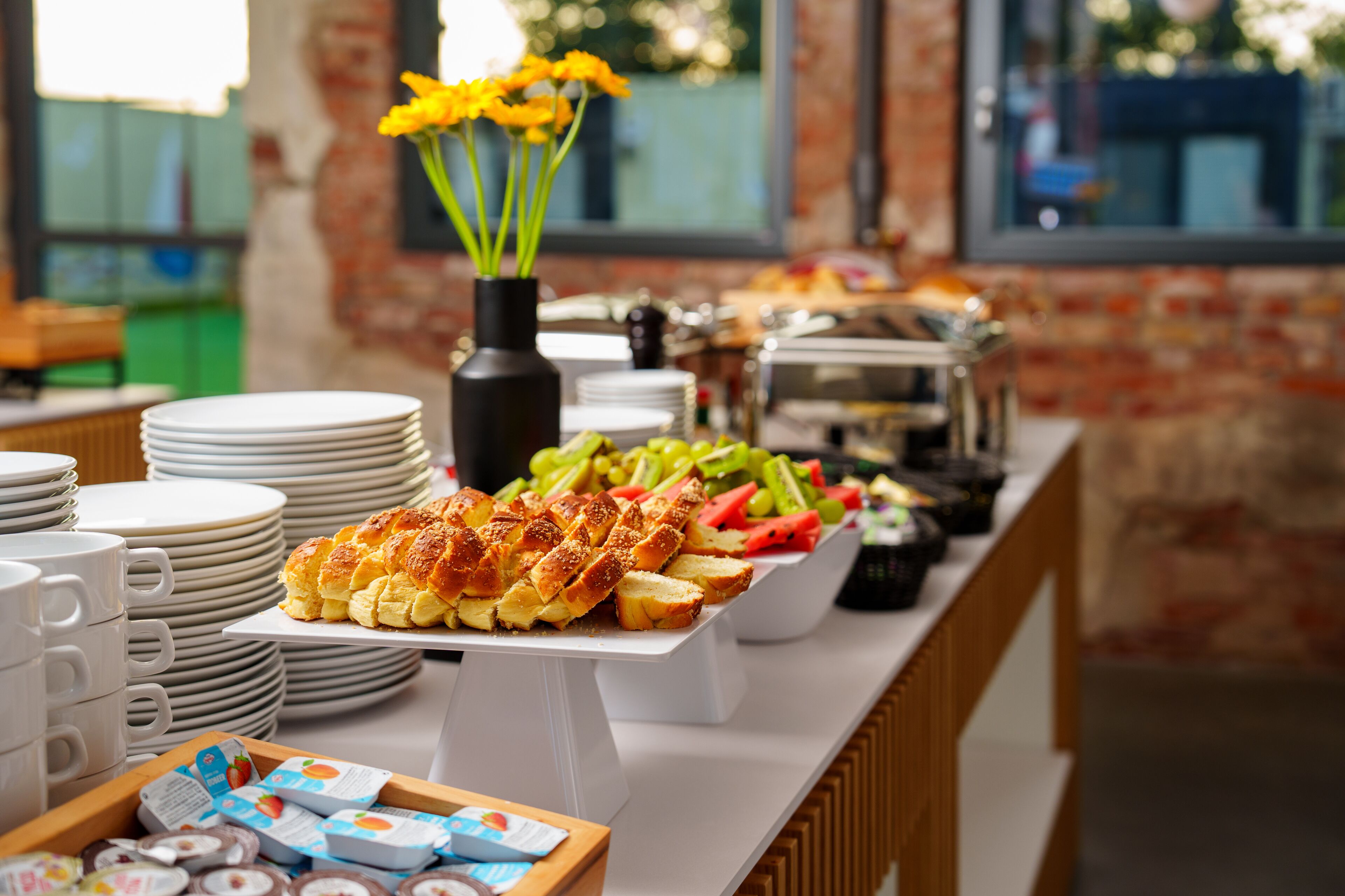 Mesa de buffet com diversos alimentos e um vaso de flores amarelas.