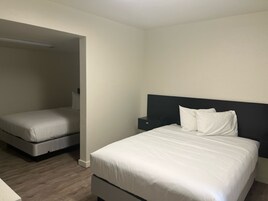 Quarto de hotel com uma cama grande, uma cama menor e uma mesa de cabeceira.