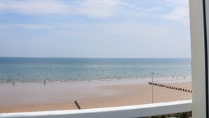 Vista da praia pela janela, com mar, areia e algumas pessoas.
