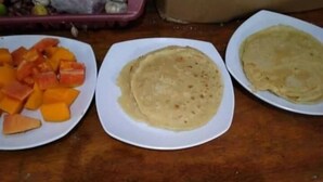 Três pratos brancos sobre uma mesa de madeira, um com manga fatiada, um com pão sírio enrolado e outro com pão sírio enrolado.