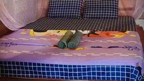Uma cama com colcha roxa, duas almofadas com padrão xadrez e uma toalha enrolada.